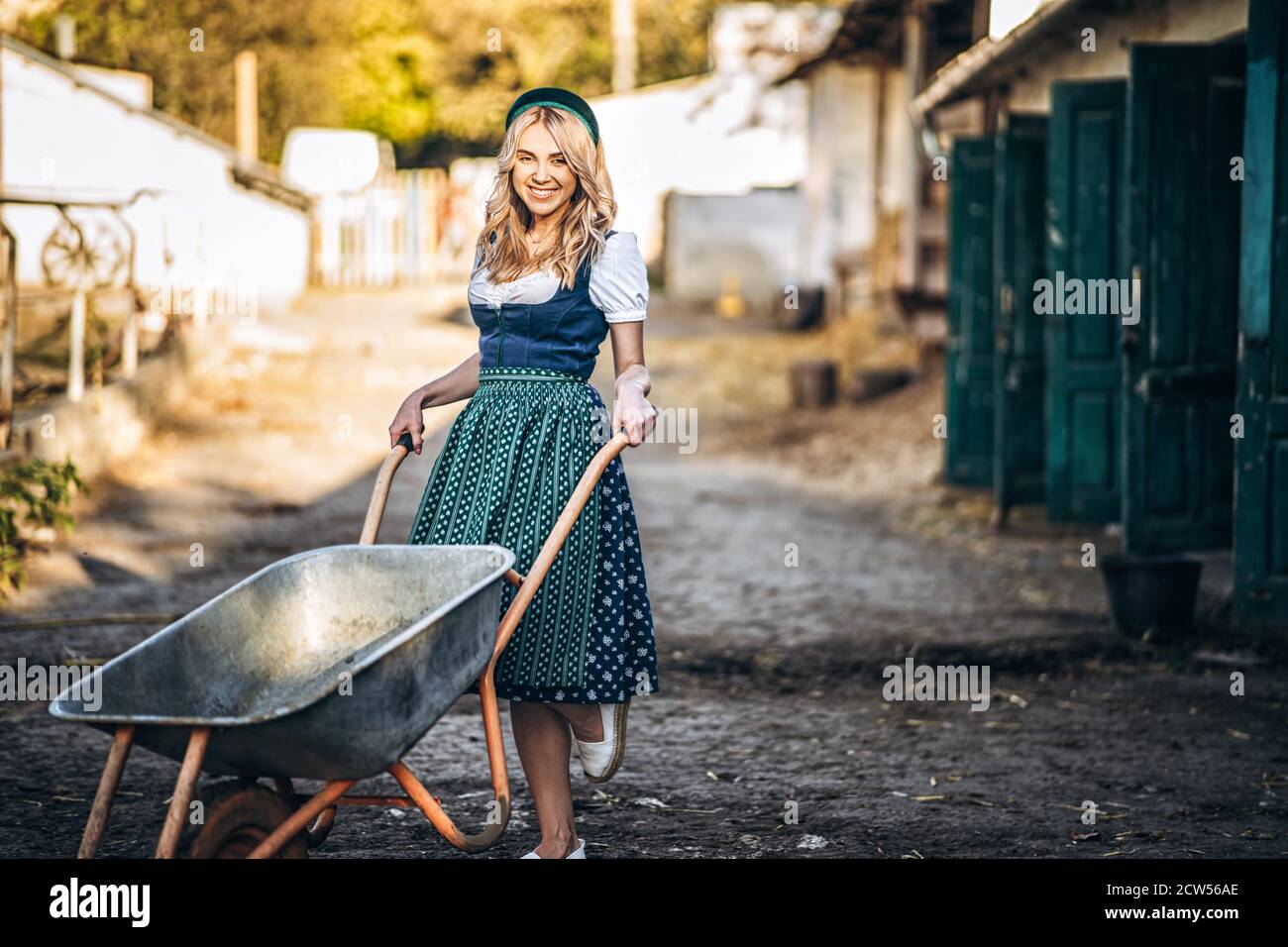 Pretty smiling blonde in traditional dress with wheelbarrow working in ...