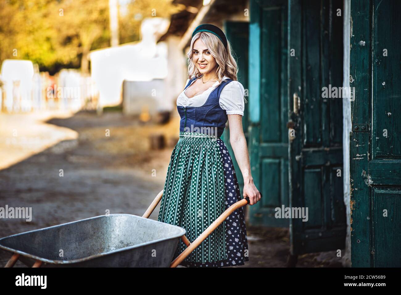 Pretty smiling blonde in traditional dress with wheelbarrow working in ...