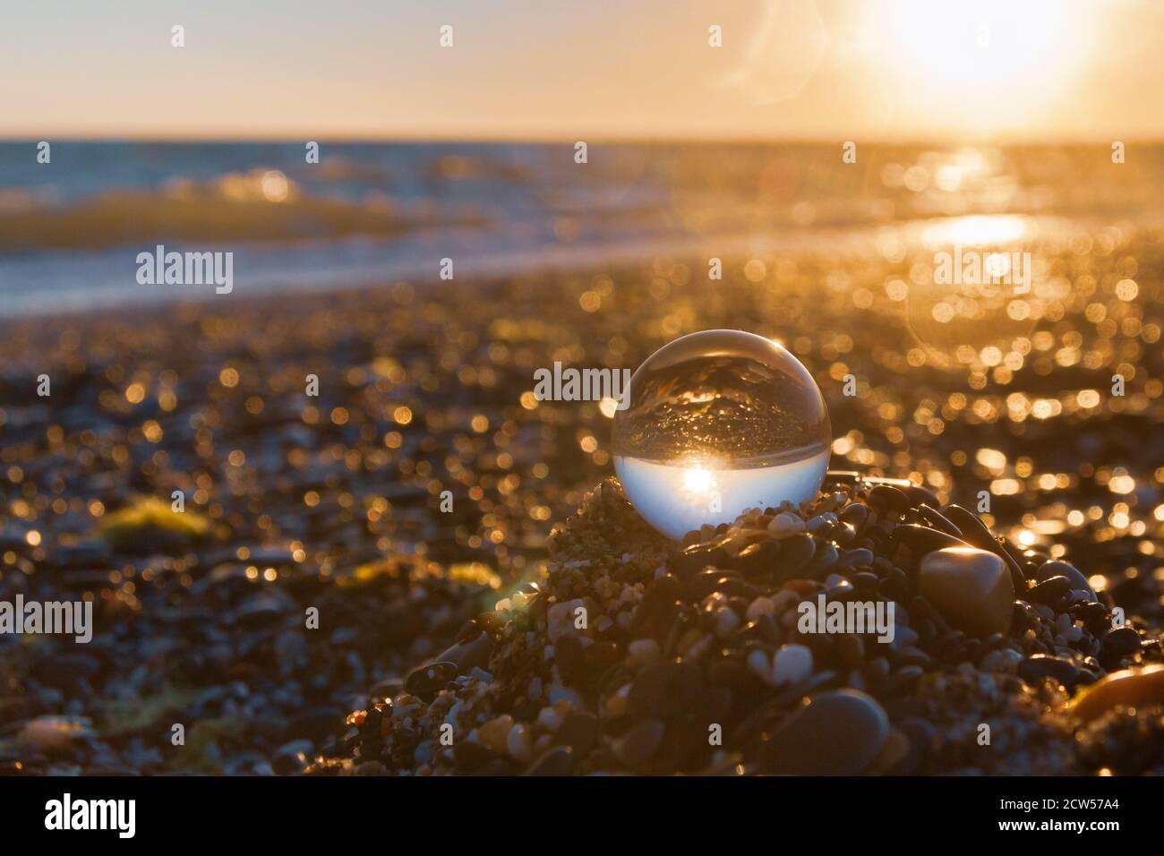Glass round ball on the beach reflects the sea in summer at sunset ...