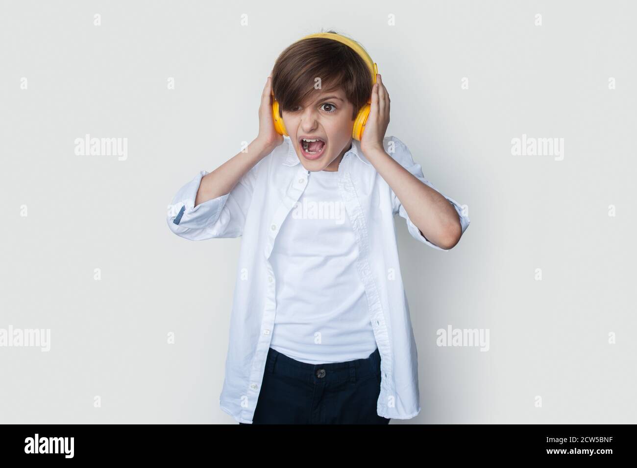 Caucasian boy screaming on a white studio wall while listening to music ...
