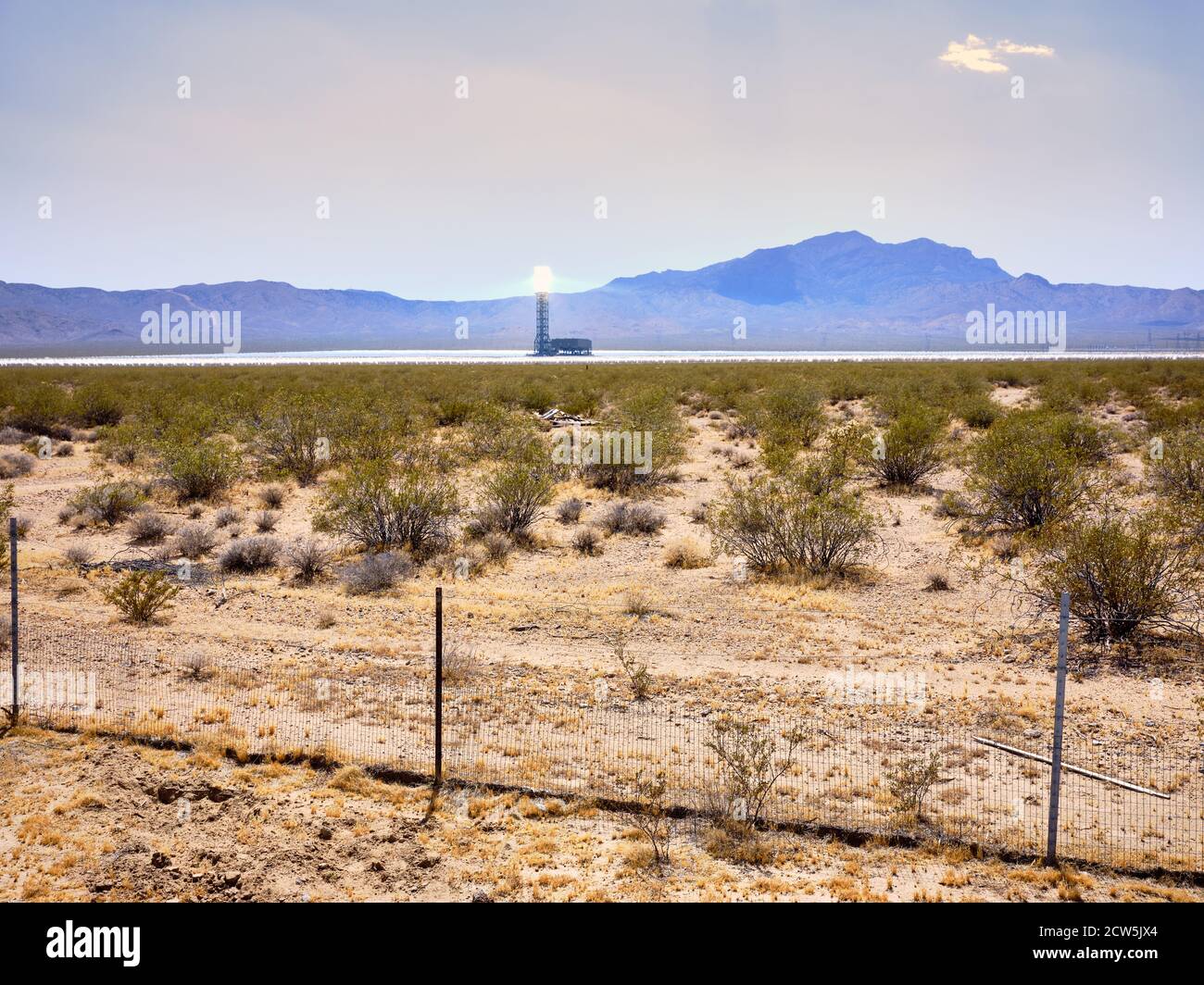 Solar tower reflects sun beams at solar farm, fenced in dirt landscape ...