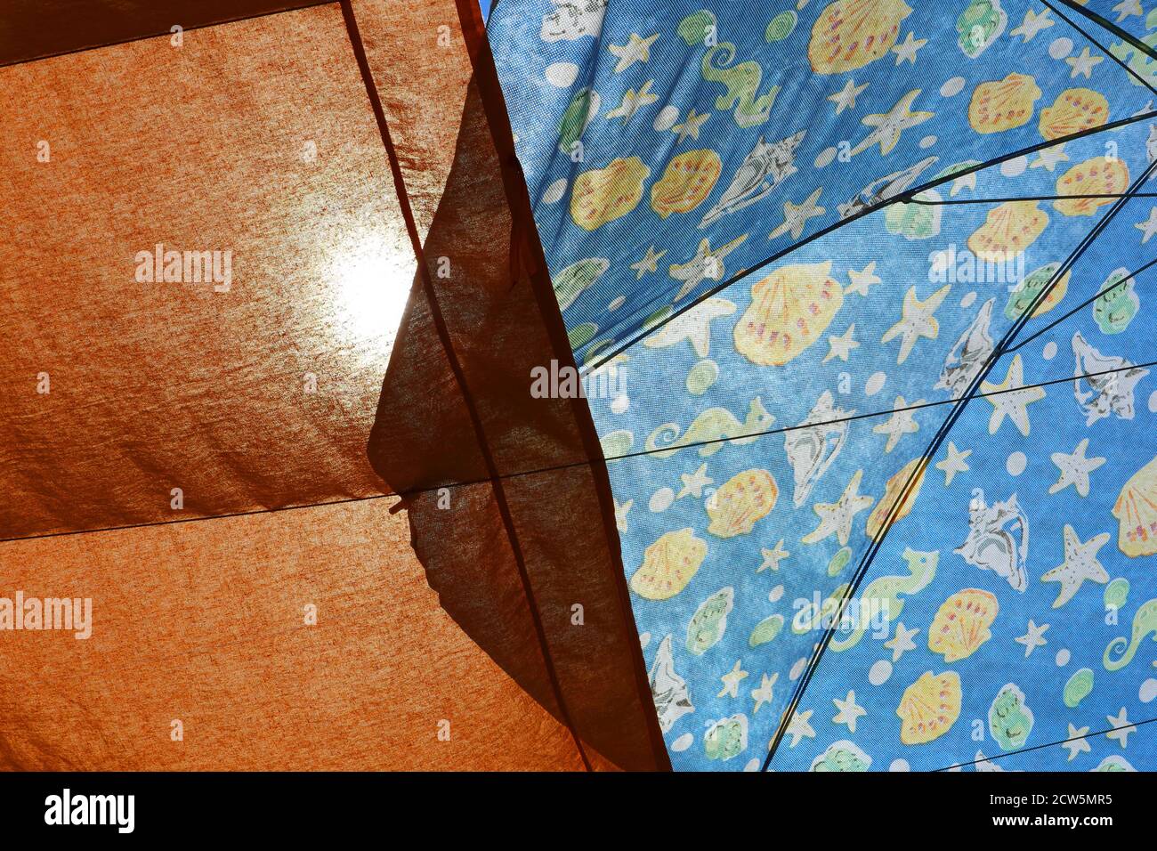 Texture of a open beach umbrella with translucent rays of blue and yel ...