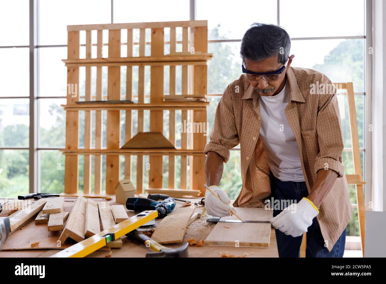 Asian senior man use ruler to measure width of wood plank in carpentry ...