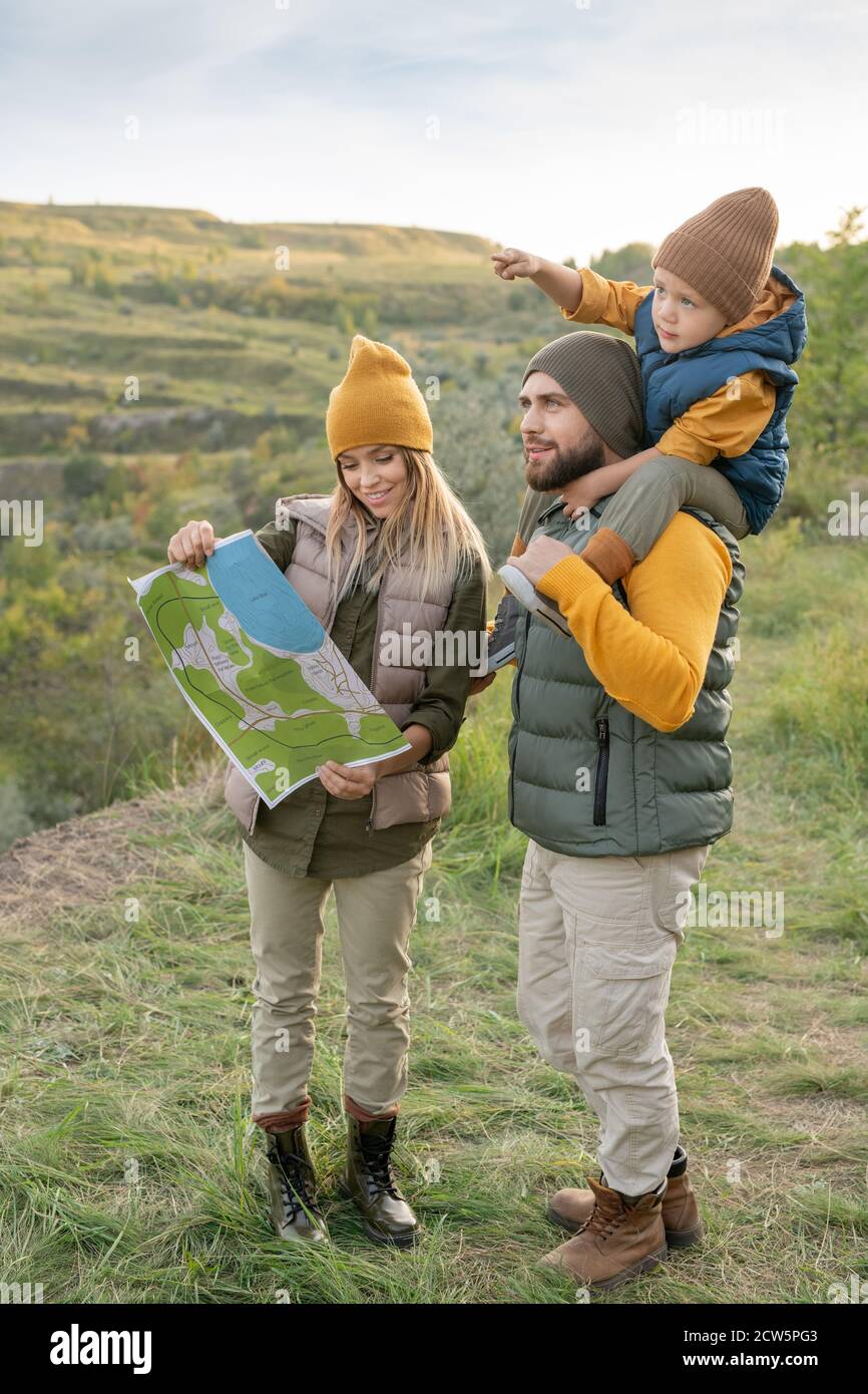 Young family of backpackers looking at map while little boy pointing ...