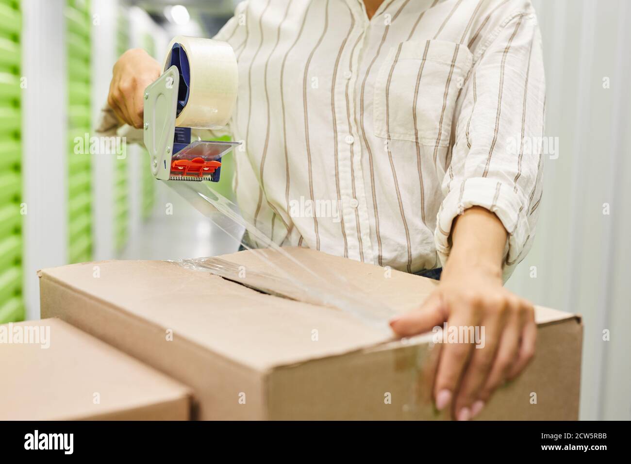 Close up of unrecognizable young woman packing boxes with tape gun ...