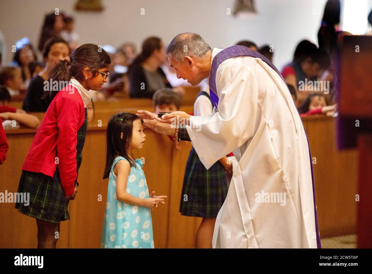 A robed deacon makes a cross of ash on a little girl's forehead during ...
