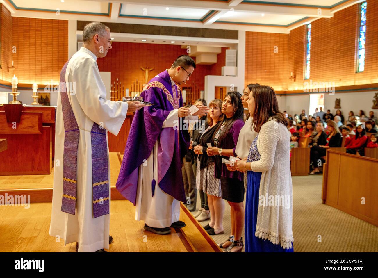 A robed deacon and an Asian American priest instruct altar assistants ...