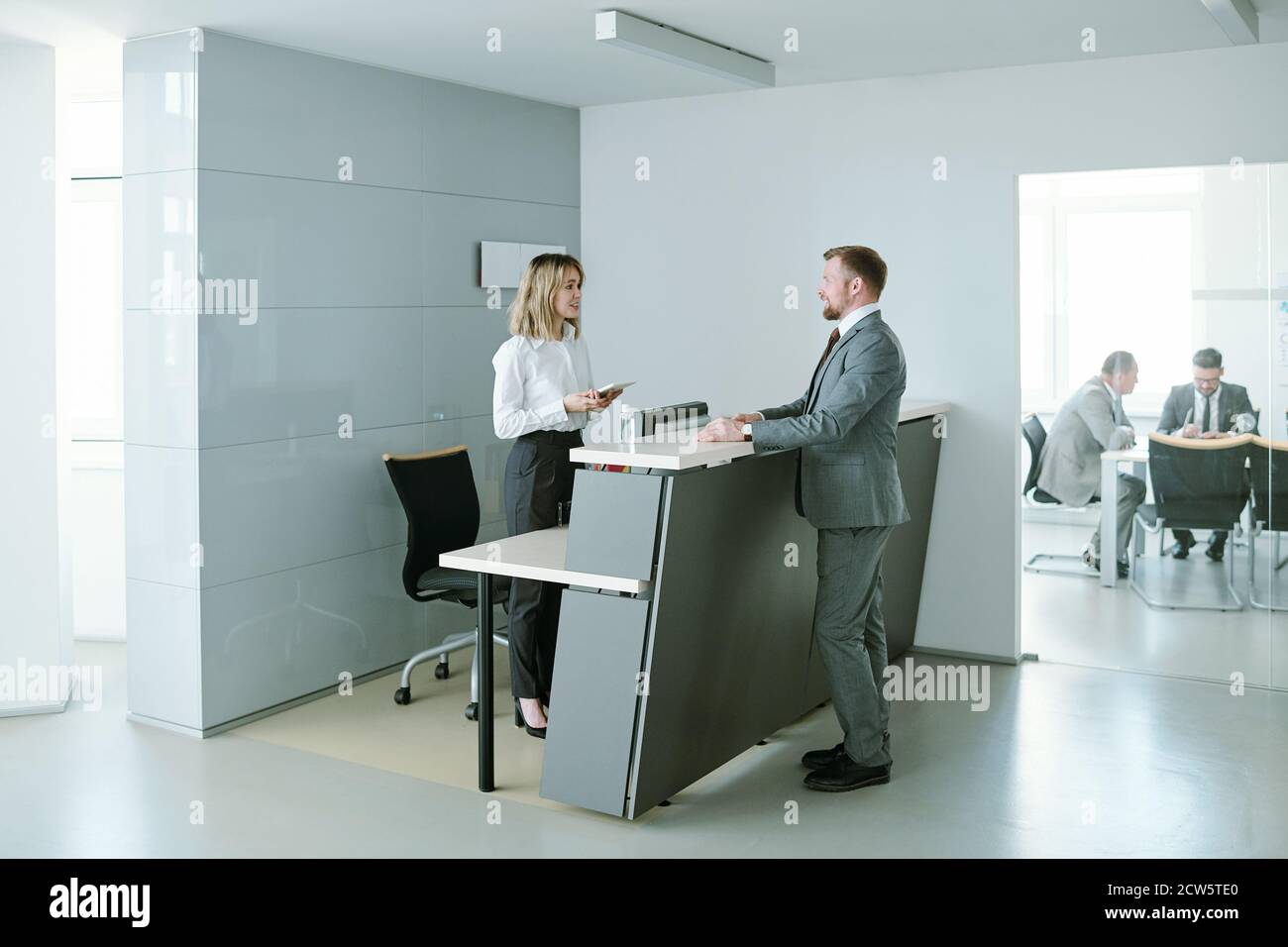 Young blond female receptionist in formalwear talking to happy ...