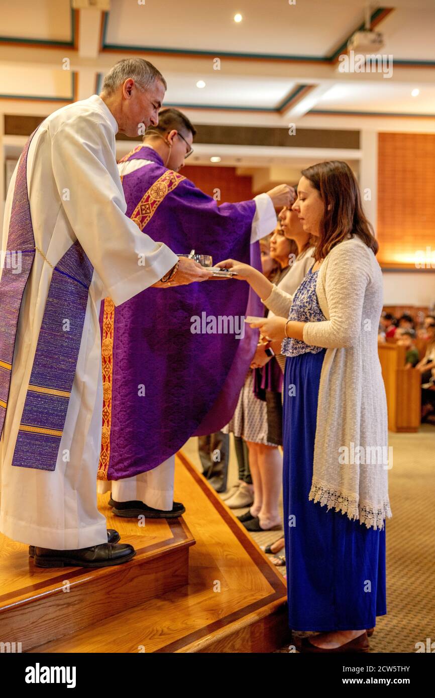 A robed deacon and an Asian American priest instruct altar assistants ...