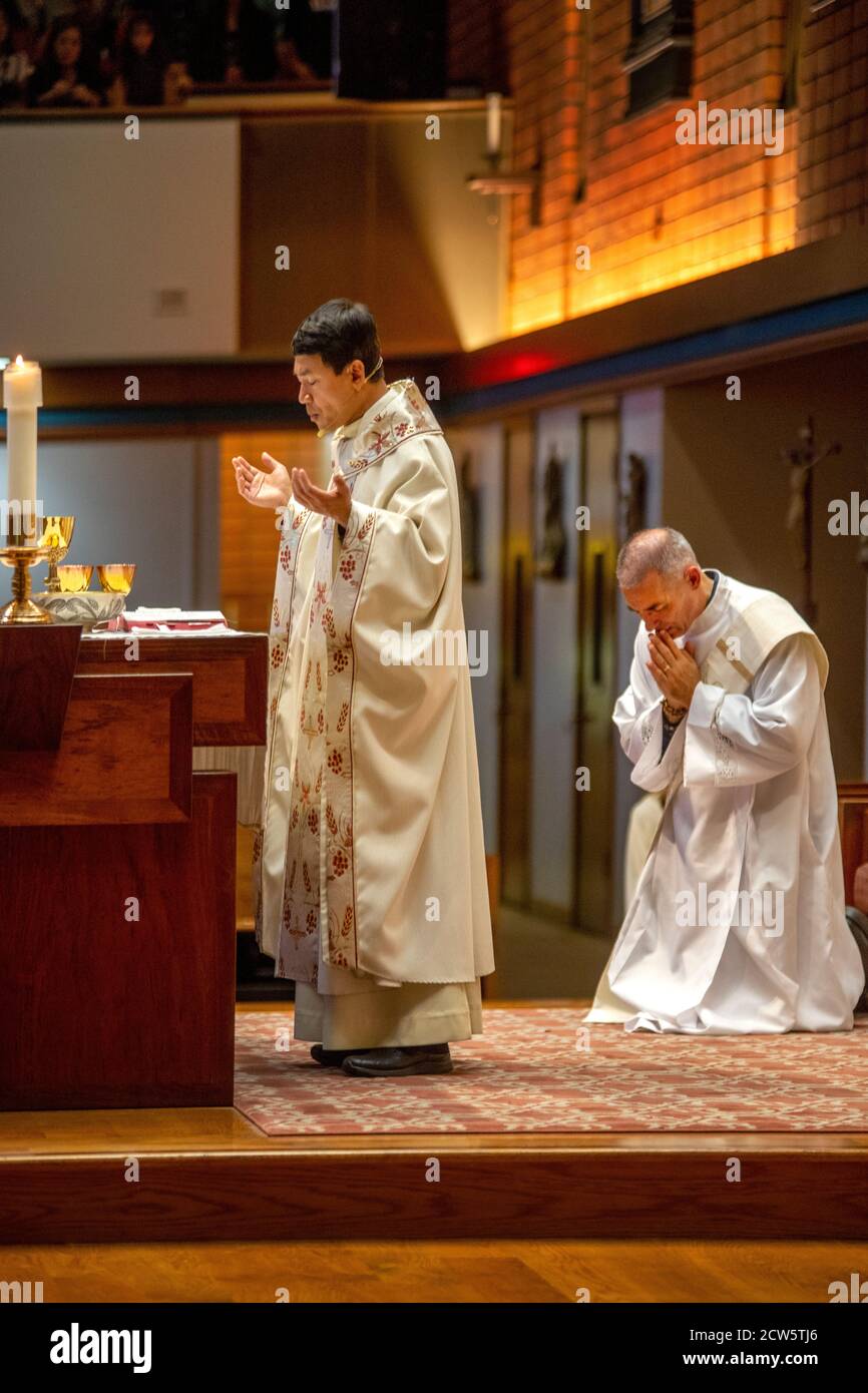 Wearing ceremonial robes, a deacon bows his head in prayer as an Asian ...