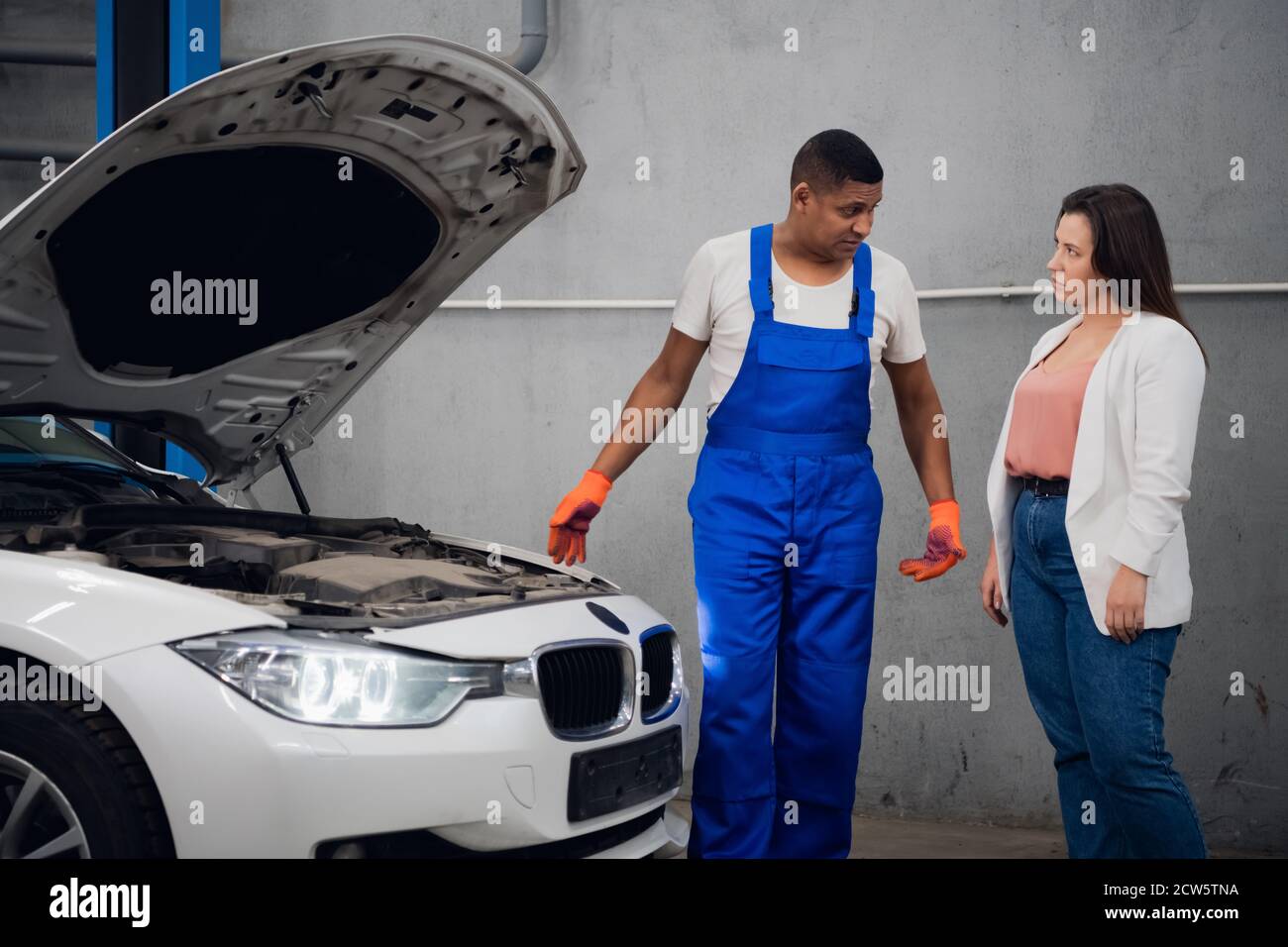 Workshop worker and woman discuss car engine repair Stock Photo - Alamy