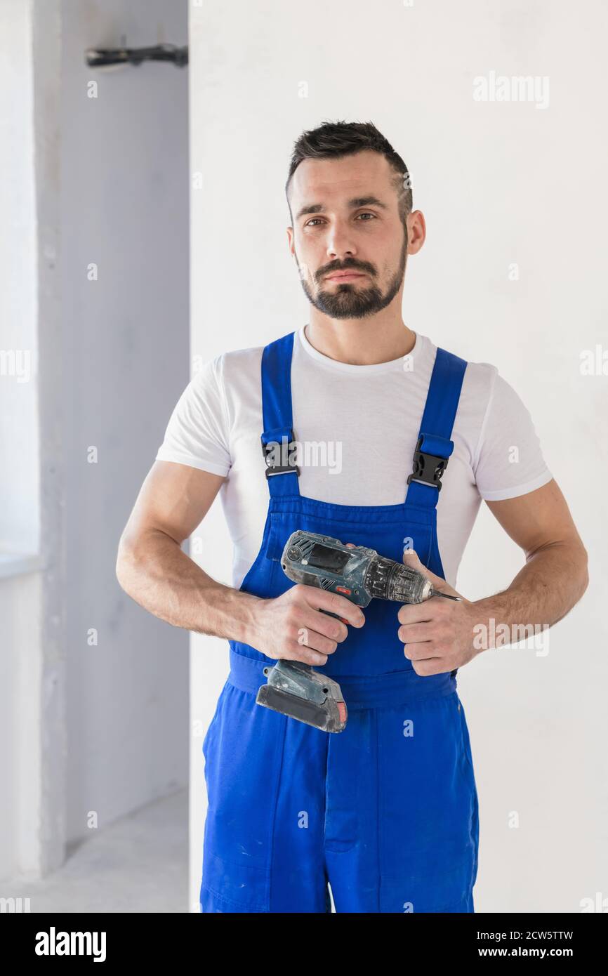 Serious builder in blue overalls posing with a drill Stock Photo - Alamy