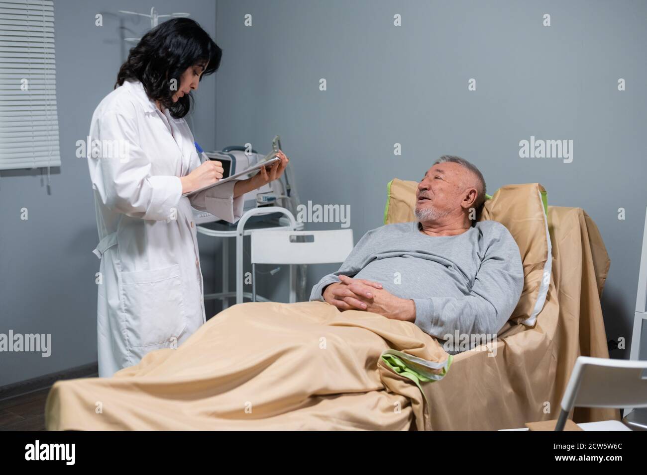 A doctor holding a clipboard and taking notes, while talking to her ...