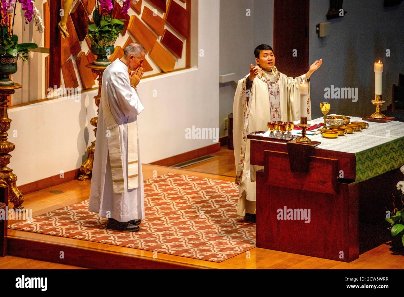 Wearing ceremonial robes, a deacon bows his head in prayer as an Asian ...