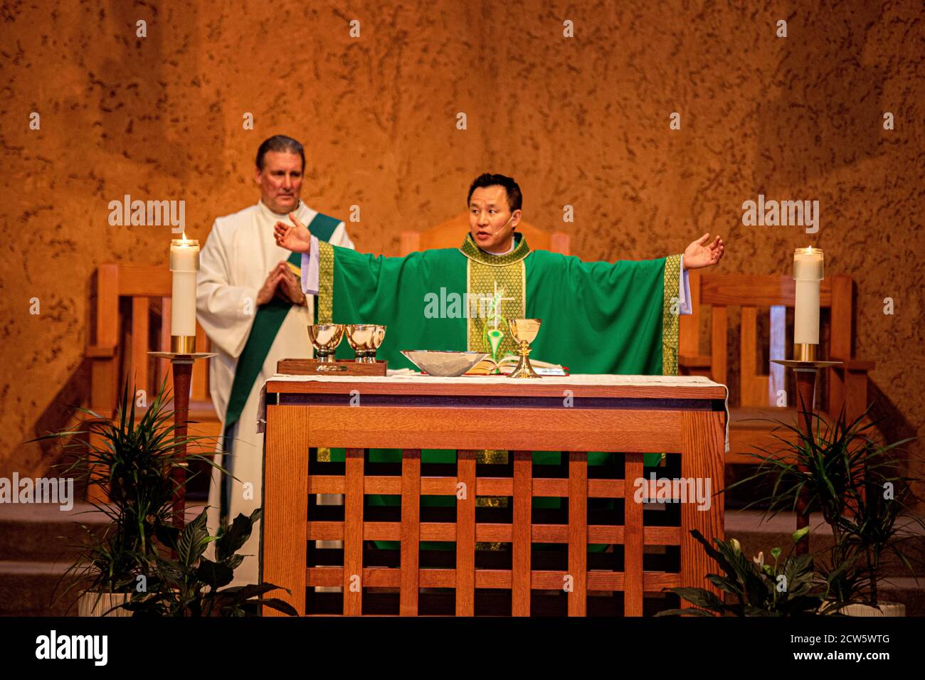 A robed deacon and an Asian American priest celebrate mass at the altar ...