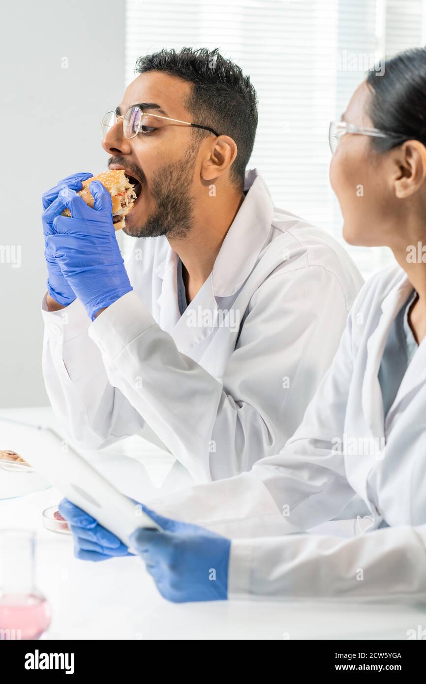 Gloved young male worker of food control biting hamburger or cheeseburger in lab Stock Photo - Alamy