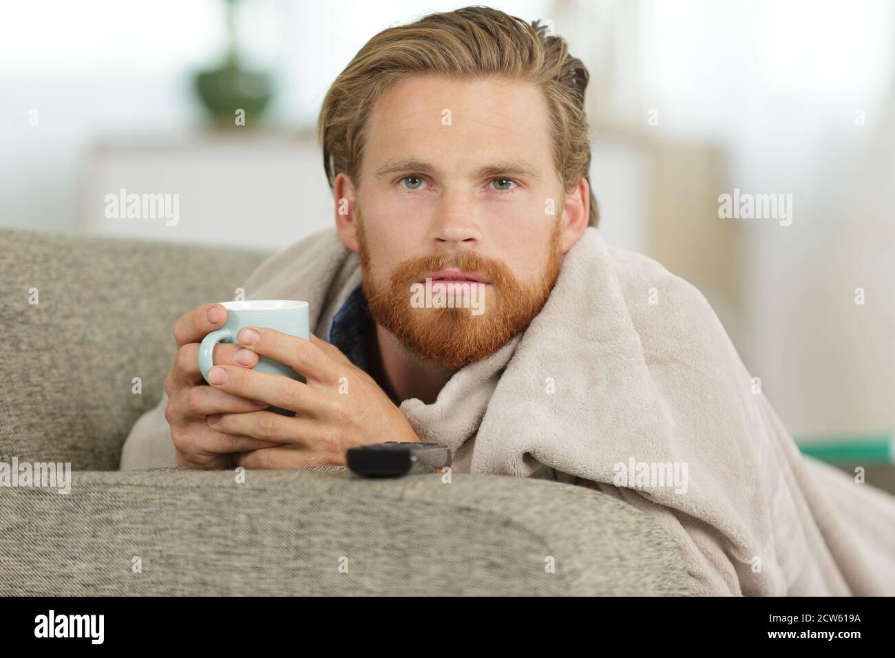 man wrapped in blanket with hot drink watching television Stock Photo ...