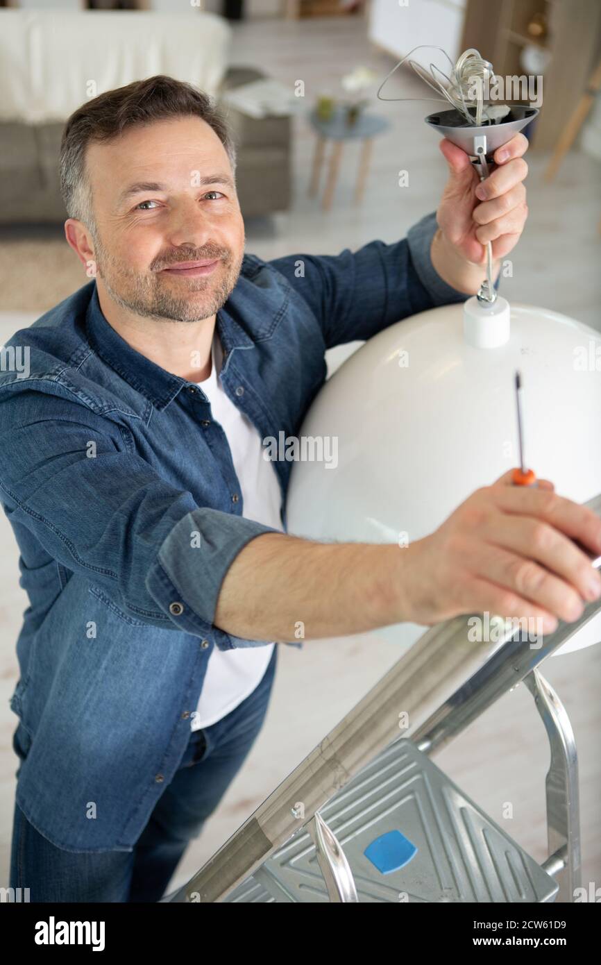 man hanging up a light with a large shade Stock Photo - Alamy