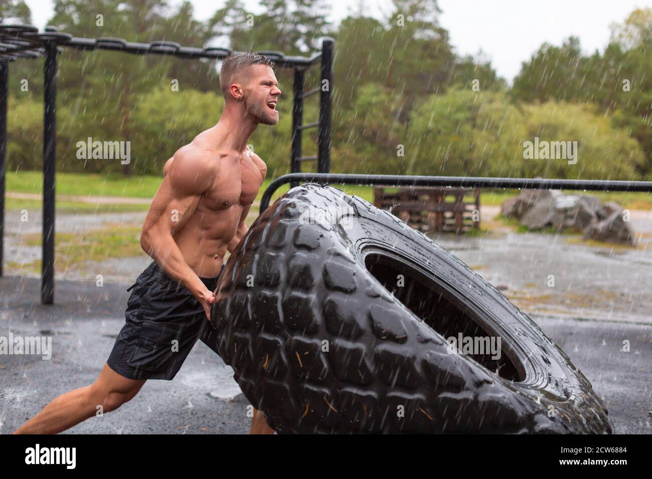 Young man flipping a tire. Heavy workout in a rainy day. Sport ...