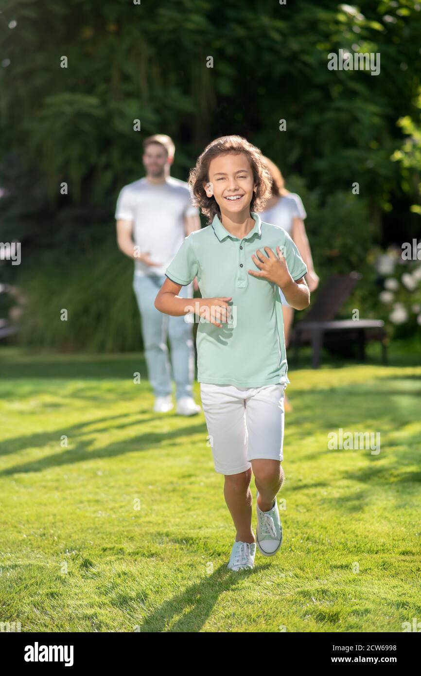 Excited boy running on lawn, his parents walking behind Stock Photo - Alamy