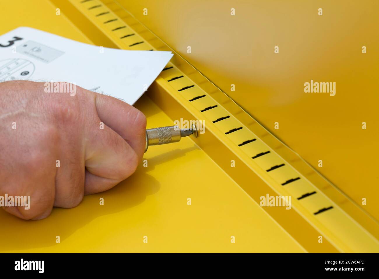 Man Assembling A Yellow Metal Cabinet With A Screwdriver And