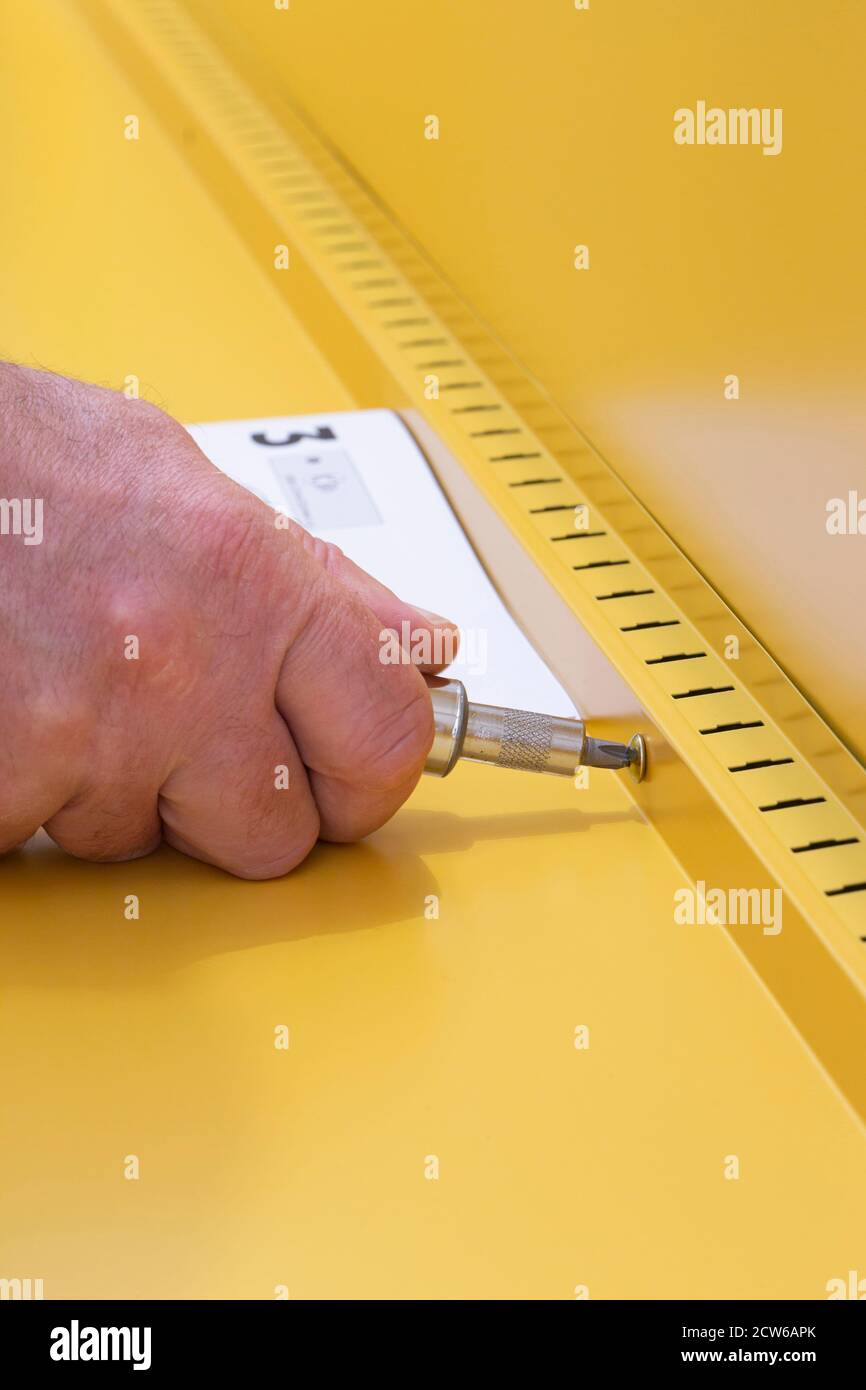 Man Assembling A Yellow Metal Cabinet With A Screwdriver And
