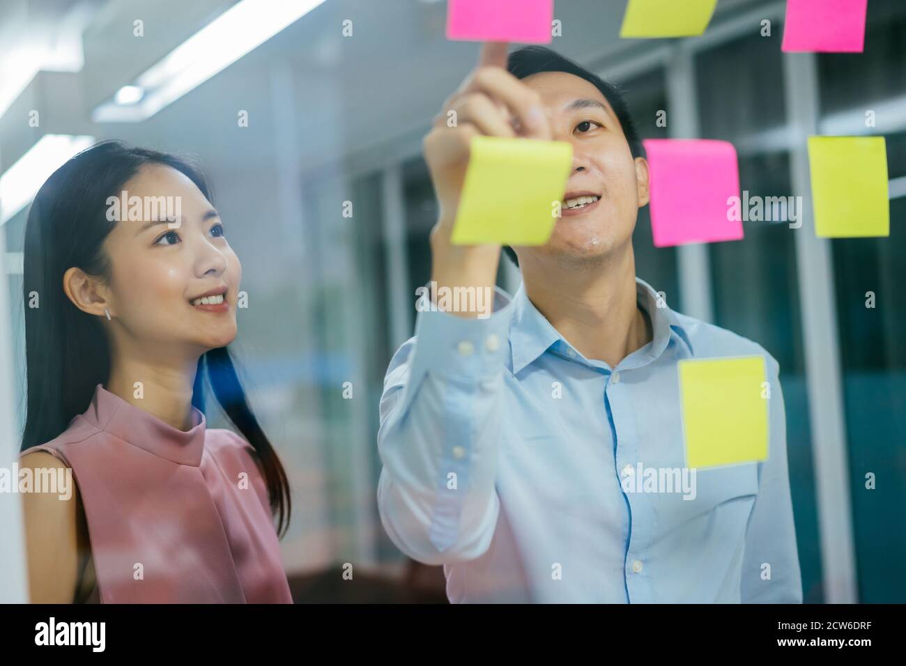 Two business coworkers sticking post it notes on glass, planning ...