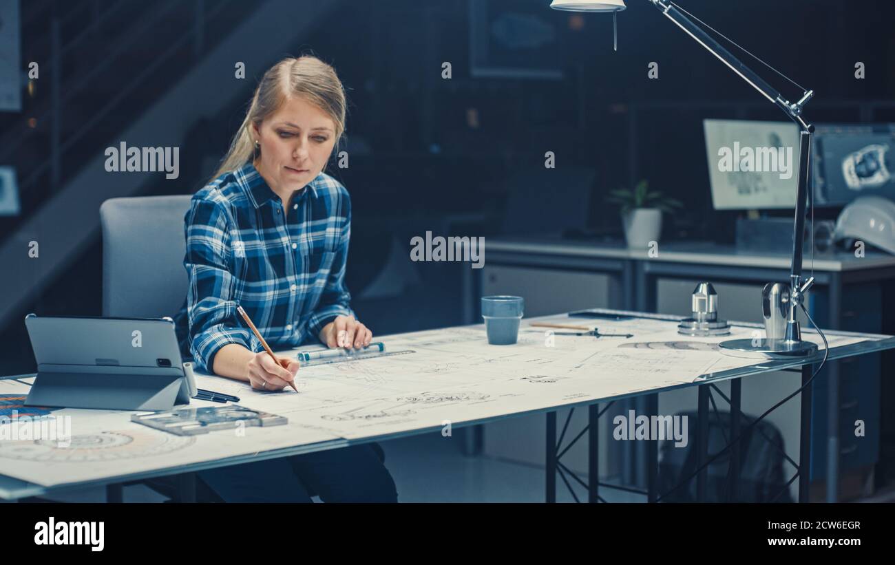 Female Engineer Sitting at Her Desk Works with Blueprints Laying on a ...