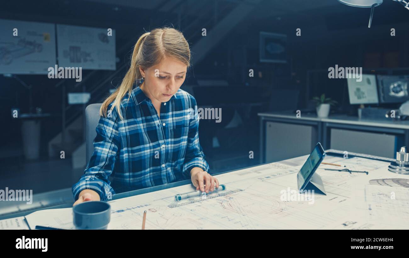 Female Engineer Sitting at Her Desk Works with Blueprints Laying on a ...