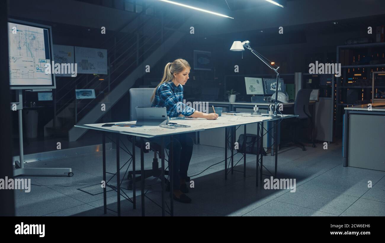 Female Engineer Sitting at Her Desk Works with Blueprints Laying on a ...