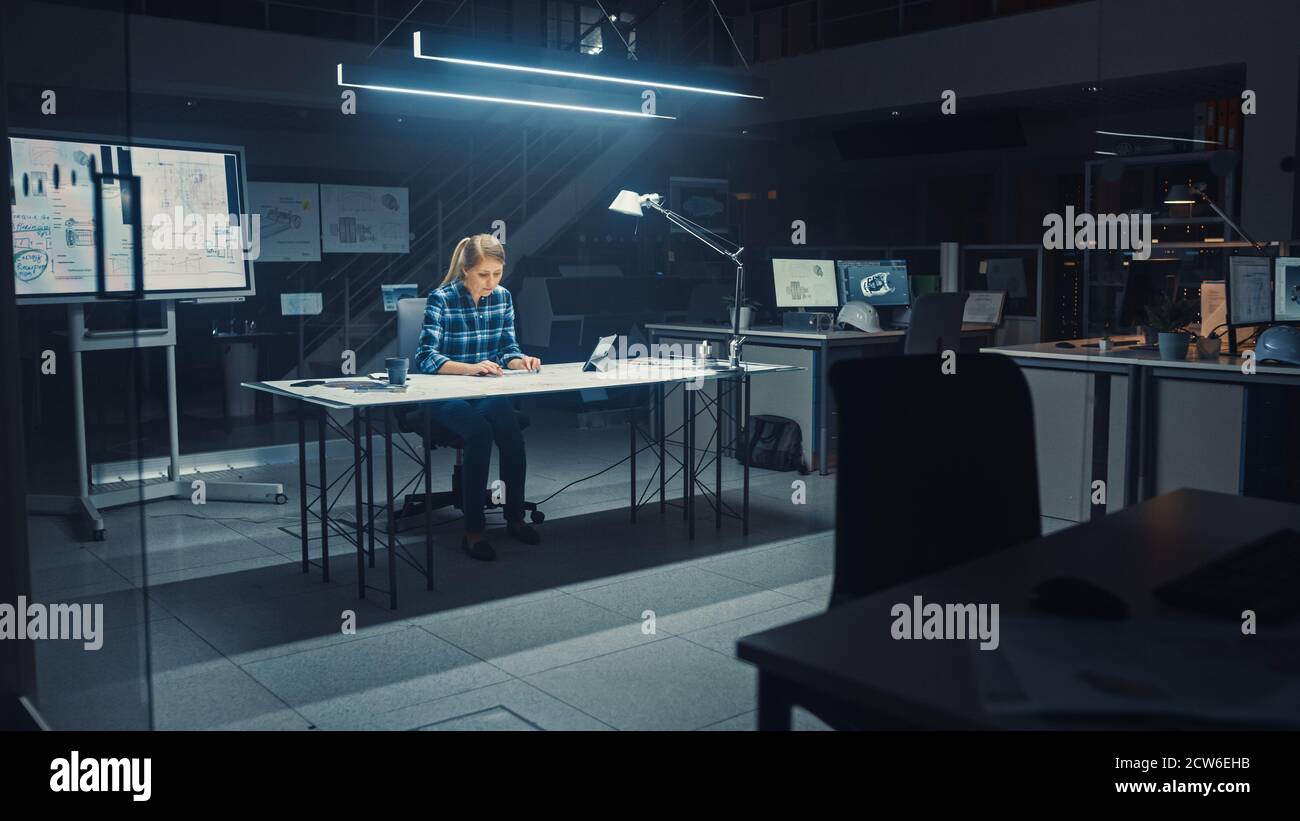 Female Engineer Sitting at Her Desk Works with Blueprints Laying on a ...