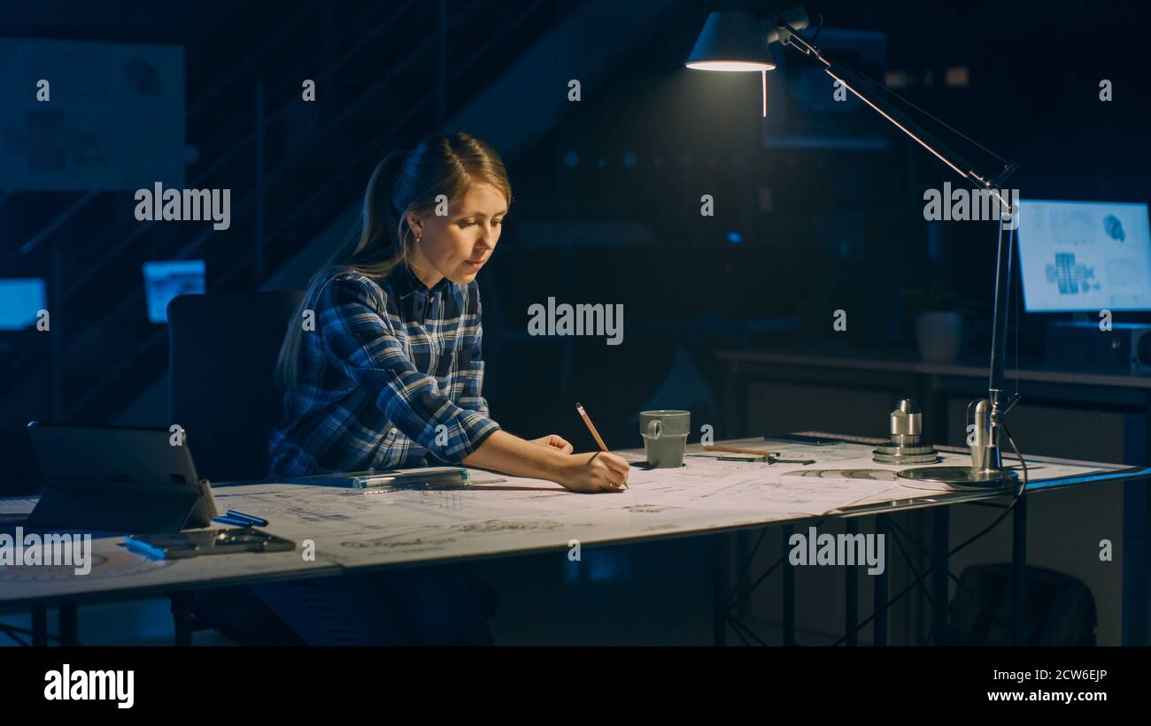 Female Engineer Sitting at Her Desk Works with Blueprints Laying on a ...
