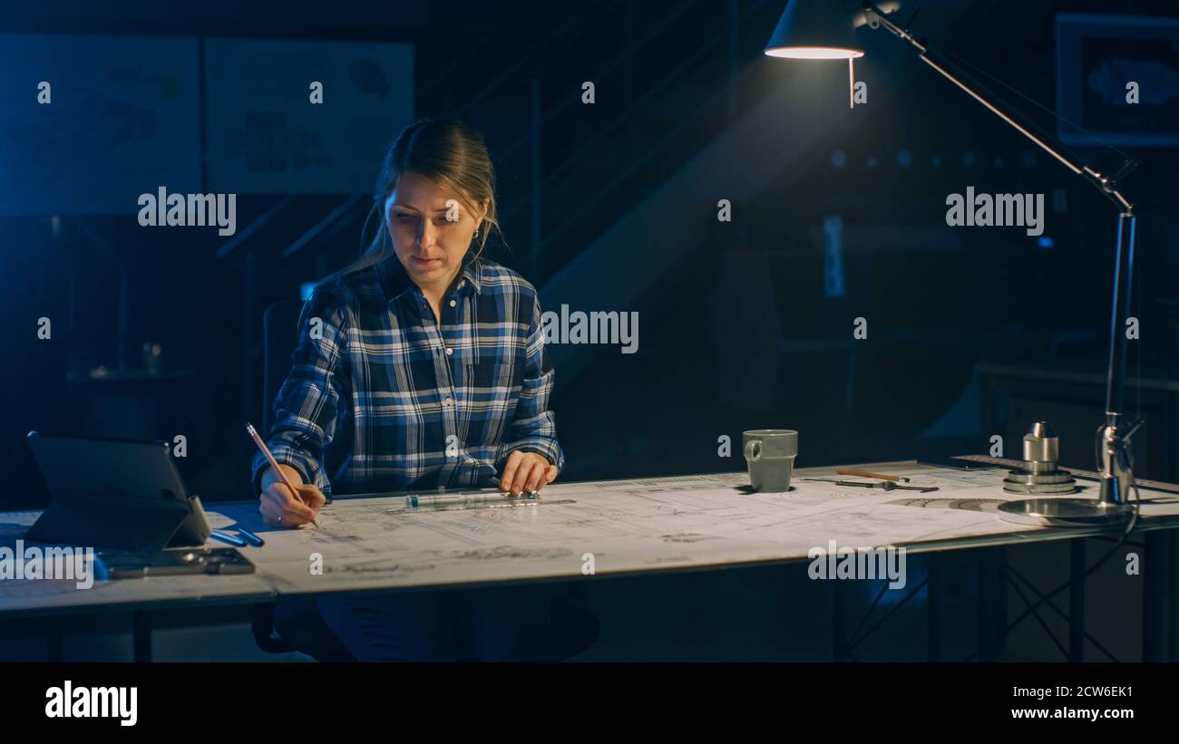 Female Engineer Sitting at Her Desk Works with Blueprints Laying on a ...