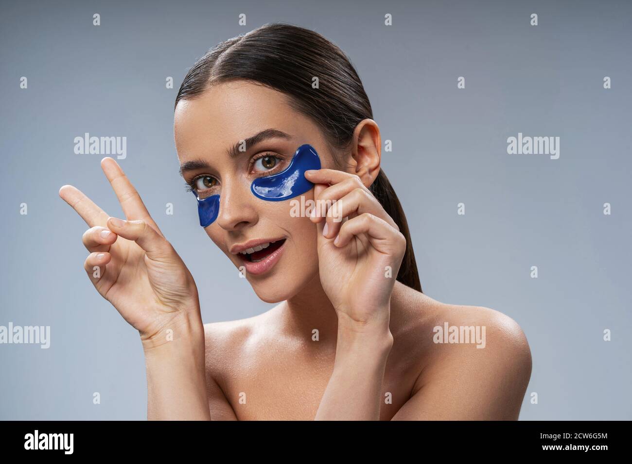 Smiling pretty lady showing victory sign on light blue background Stock ...