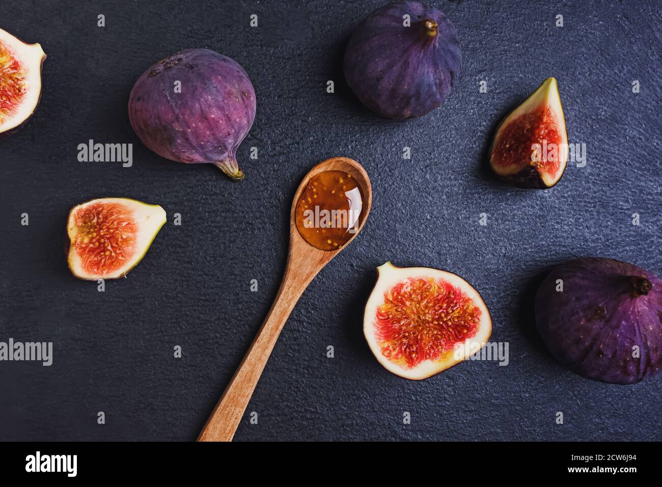 Fig jam in a wooden spoon and fresh figs on black stone background, top ...