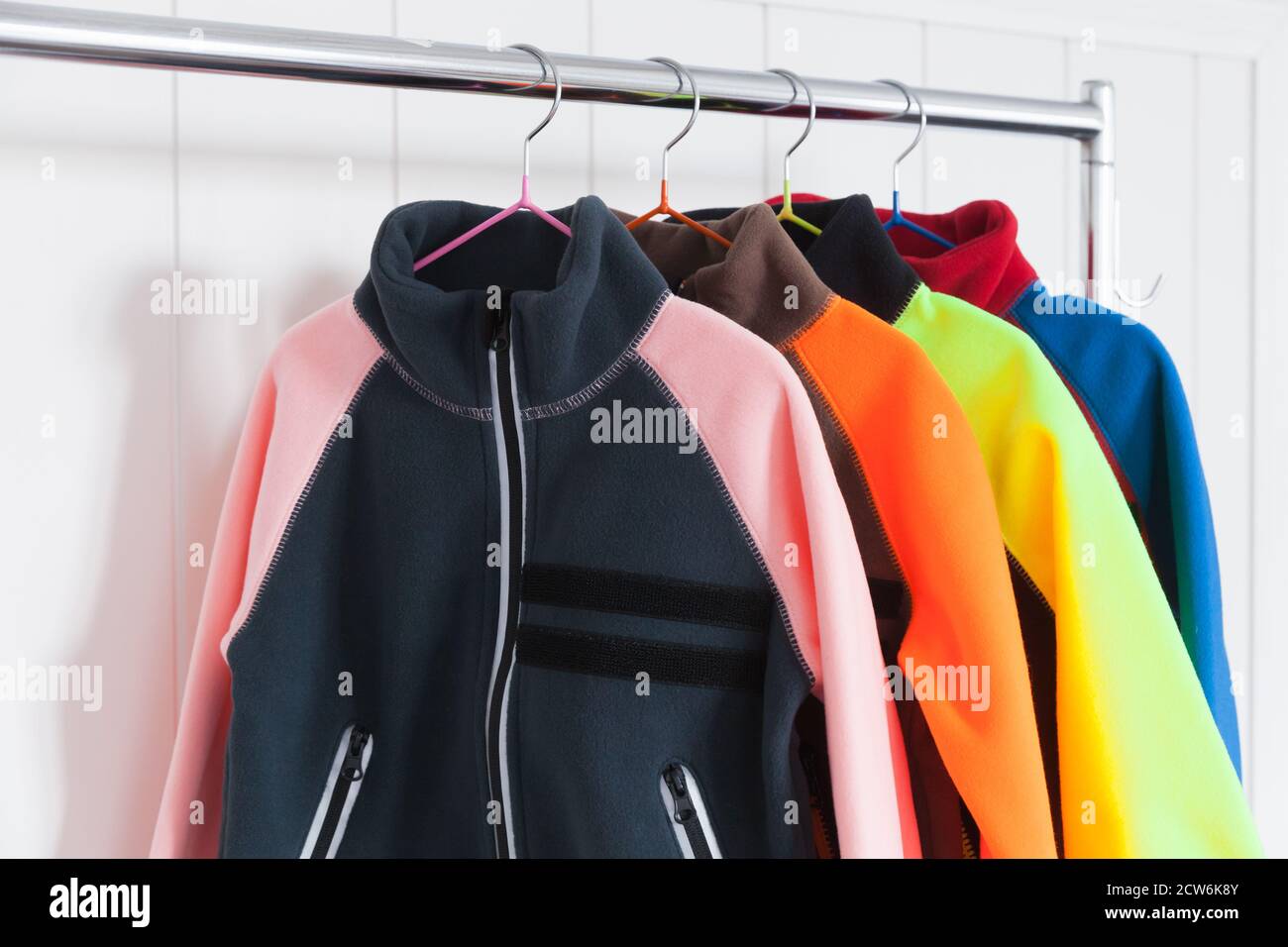 Colorful fleece jackets are on a rack near white wall Stock Photo - Alamy