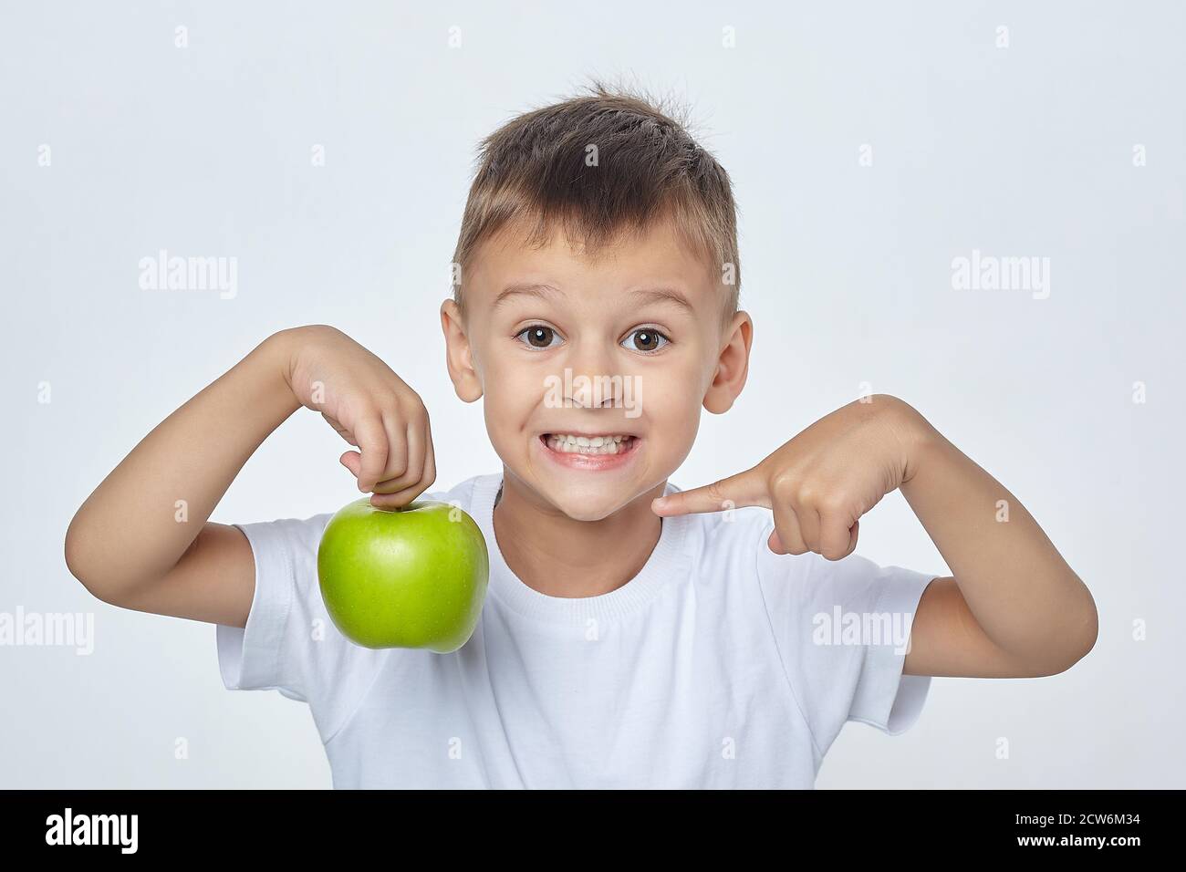 small boy with a smile holds a green Apple and points at it with his ...