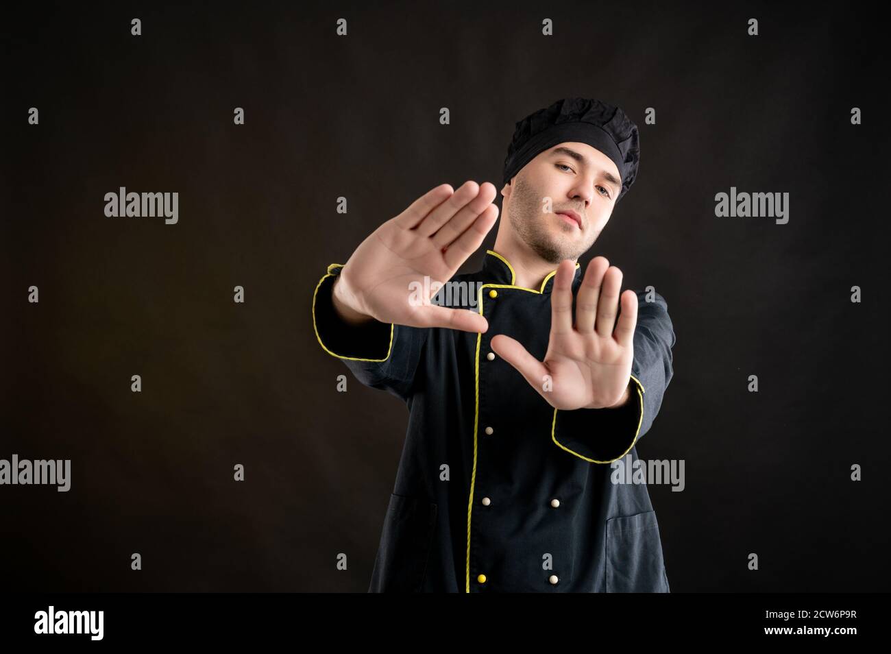Portrait of young male dressed in a black chef suit showing stop sign ...
