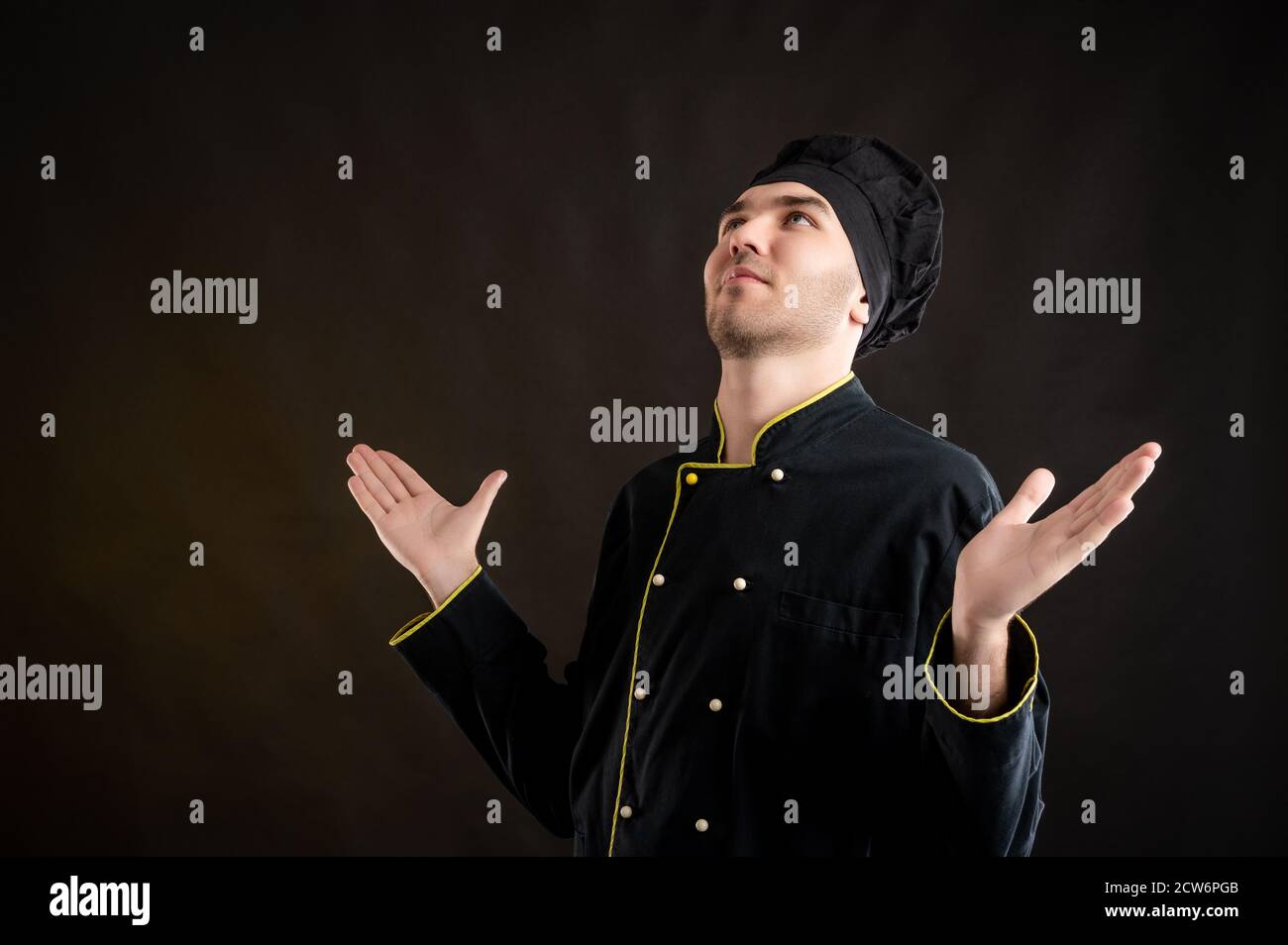 Portrait of young male dressed in a black chef suit with open arms ...