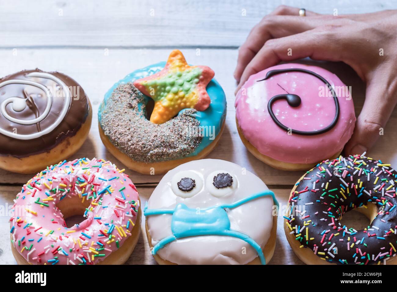 a hand picking up a donuts one of them with a handmade face mask due to ...
