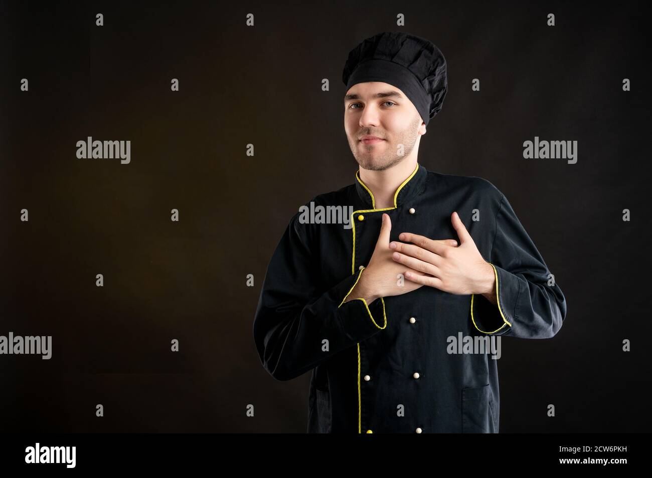Portrait of young male dressed in a black chef suit holds his hands on ...