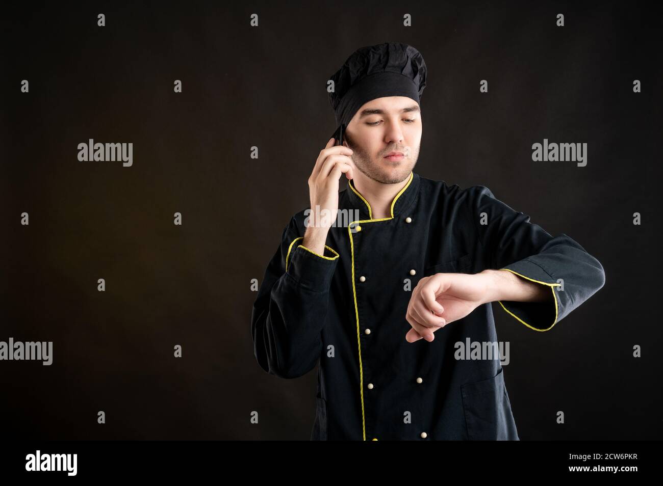 Portrait of young male dressed in a black chef suit showing it's time ...