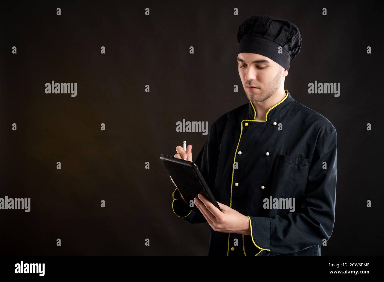 Portrait of young male dressed in a black chef suit takes notes, posing ...