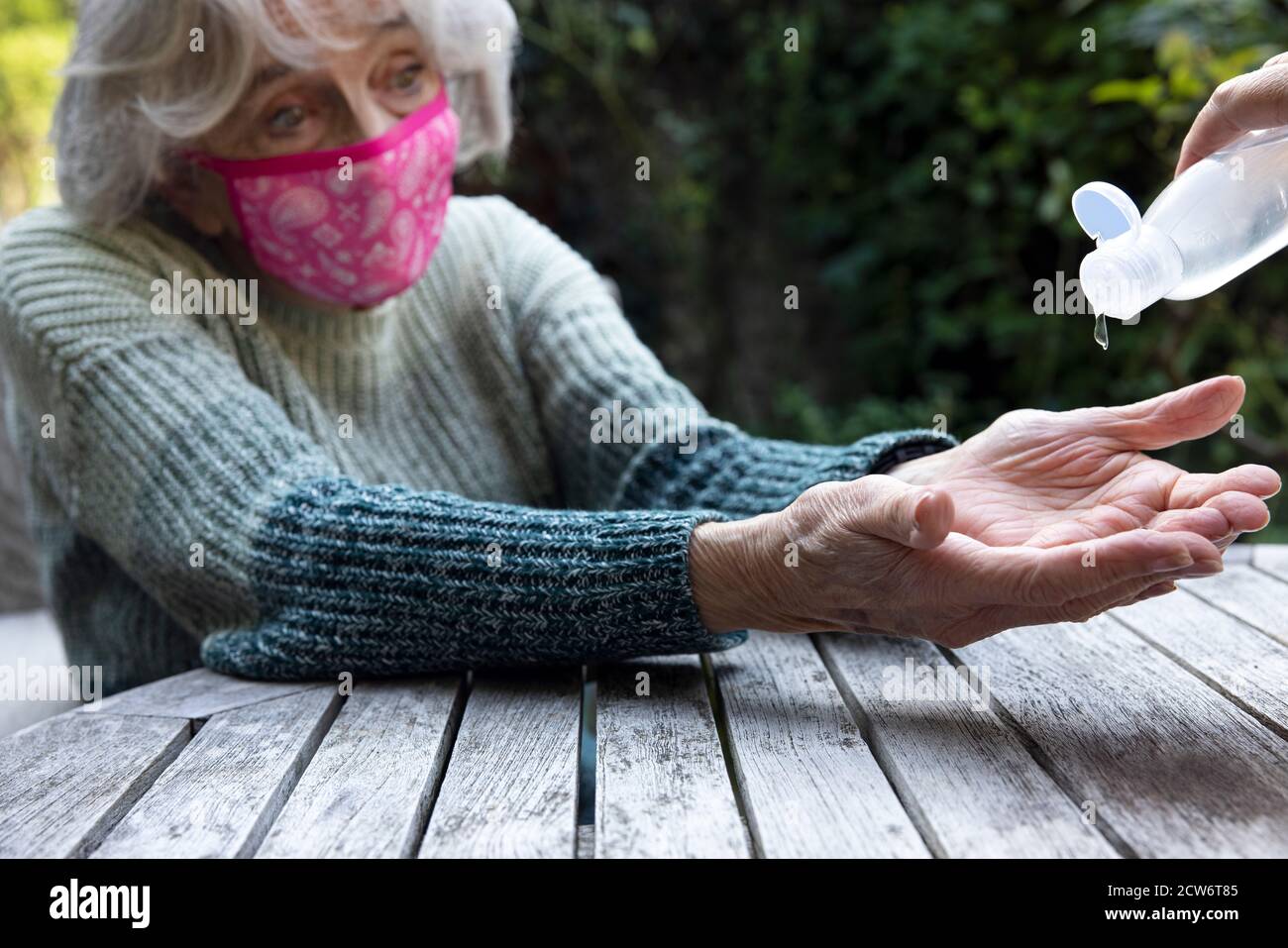 Woman Giving Hand Sanitizer To Senior Female Wearing Mask At Socially ...