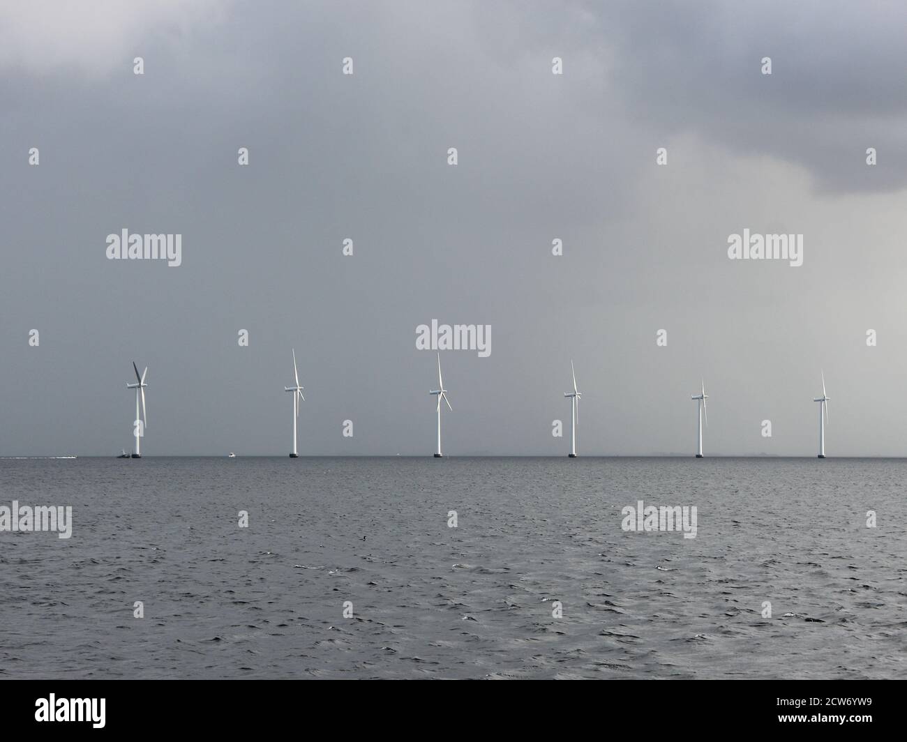 A row of white windmills on the ocean in the horizon. The colors are ...