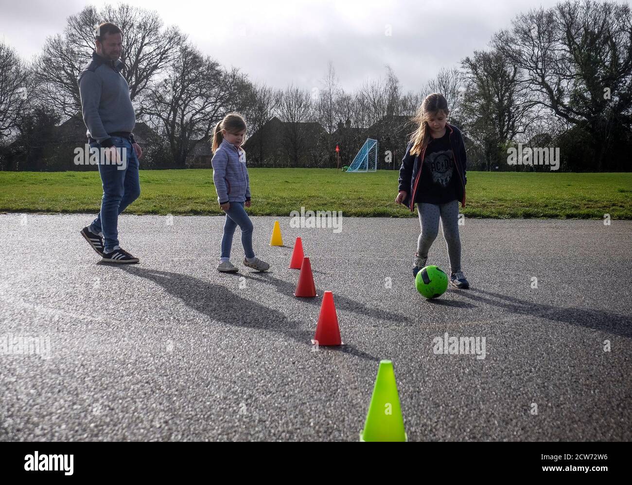 Father watching daughter practising dribbling ball around cones Stock ...