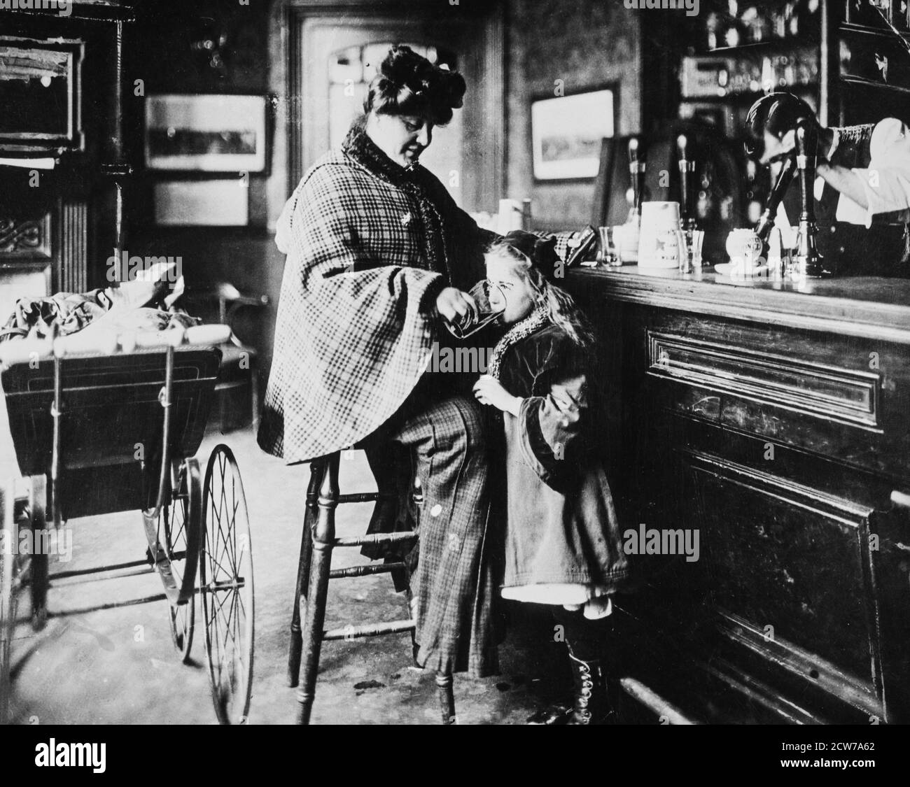 A scene inside a British pub, c 1910 A mother gives her daughter a sip ...