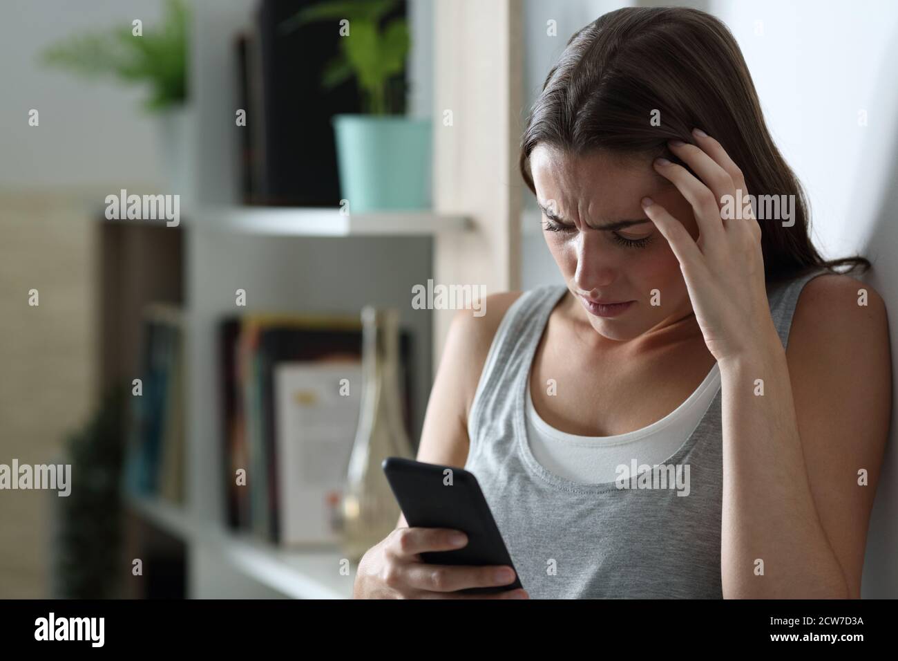 Sad teen checking smart phone content leaning in a wall at home in the ...