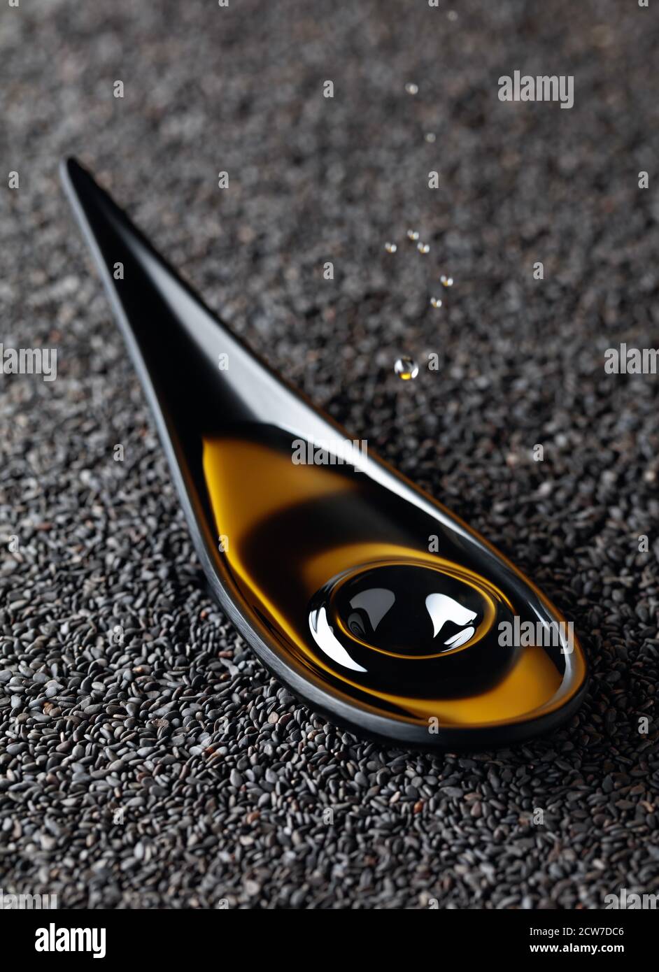 Sesame oil and raw black sesame seeds. A drop of oil fall in a small ...