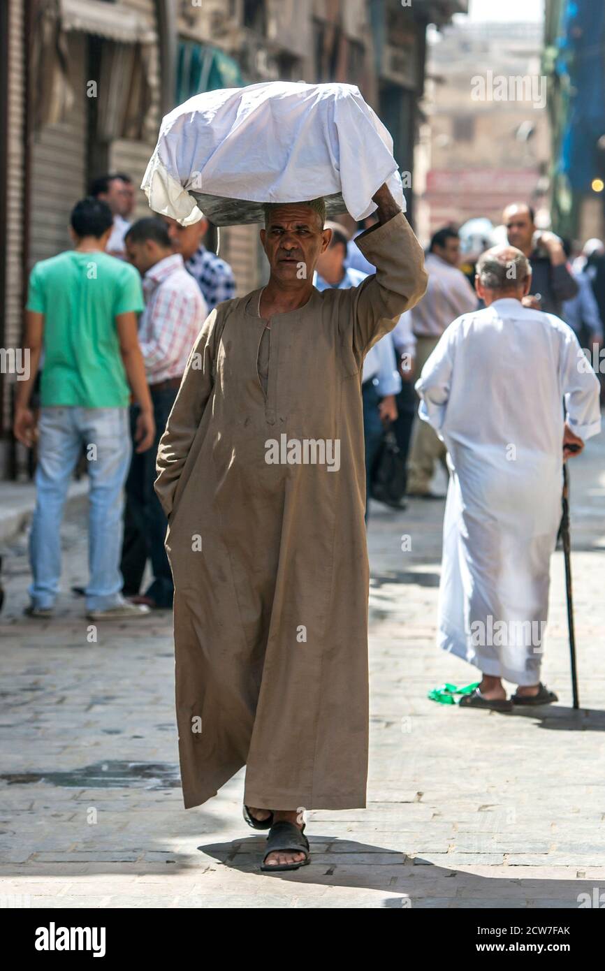 An Egyptian man carrying a load of goods on his head walks through the ...
